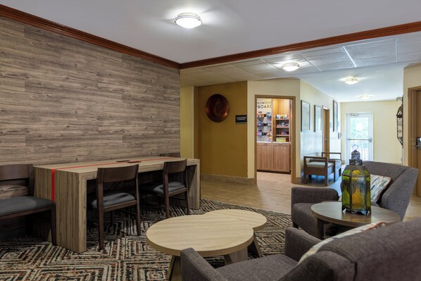 Um lobby moderno com parede de destaque em madeira, um espaço para café e áreas de estar confortáveis.