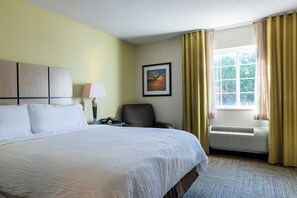Quarto de hotel com cama, poltrona, escrivaninha com luminária, quadro na parede e janela com cortinas.