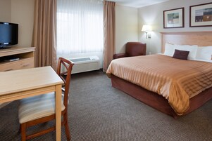 Quarto de hotel com cama, escrivaninha, cadeira, televisão e ar condicionado.