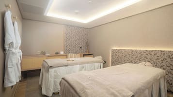 Um espaço de spa com duas macas de massagem, uma toucador com espelho e uma parede com papel de parede floral.