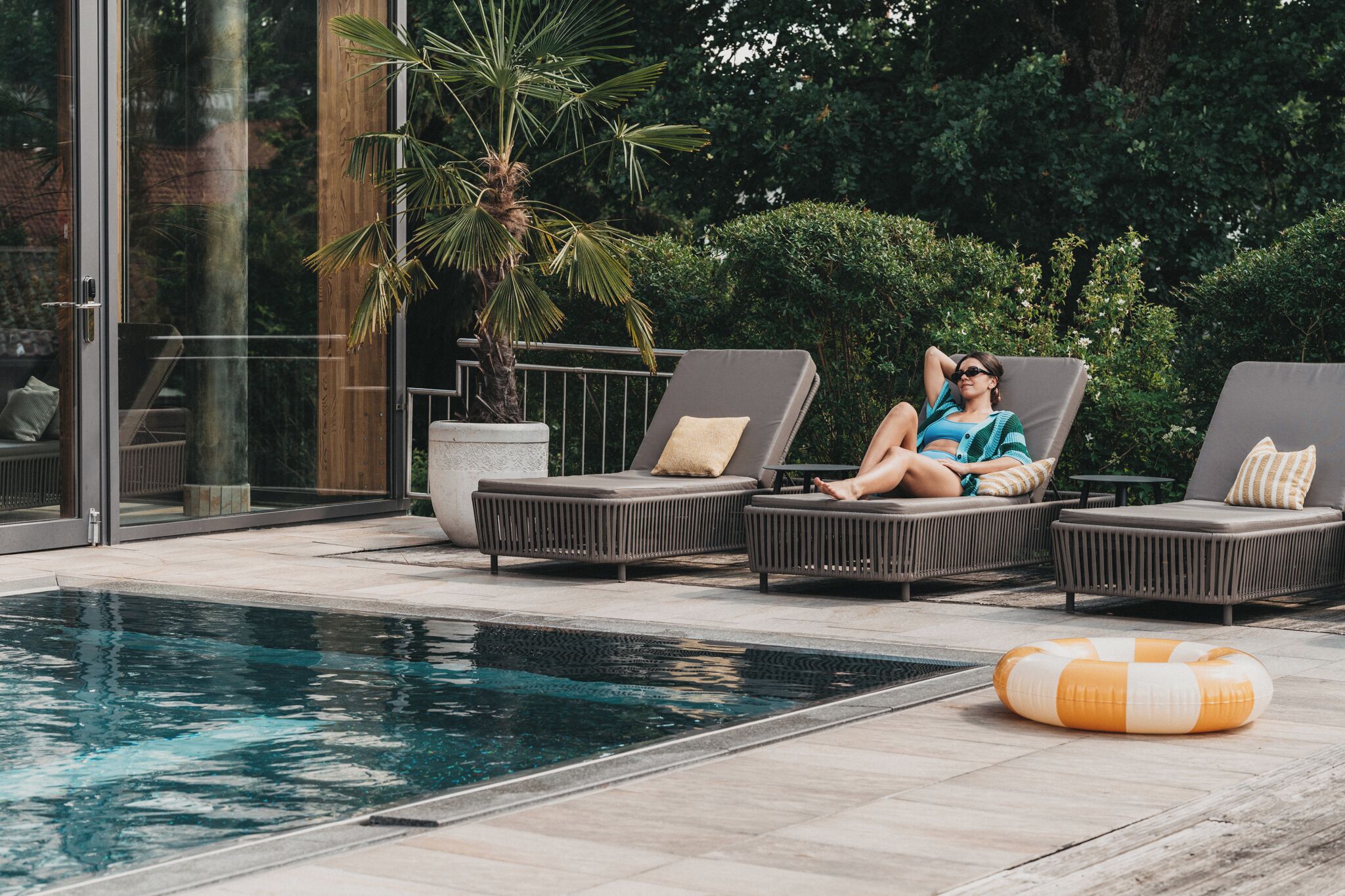Área da piscina com espreguiçadeiras, uma palmeira e vista clara da piscina.