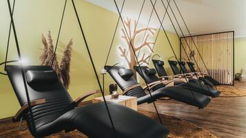 Um quarto com várias cadeiras de massagem, piso de madeira e uma parede amarela com um mural de árvore.