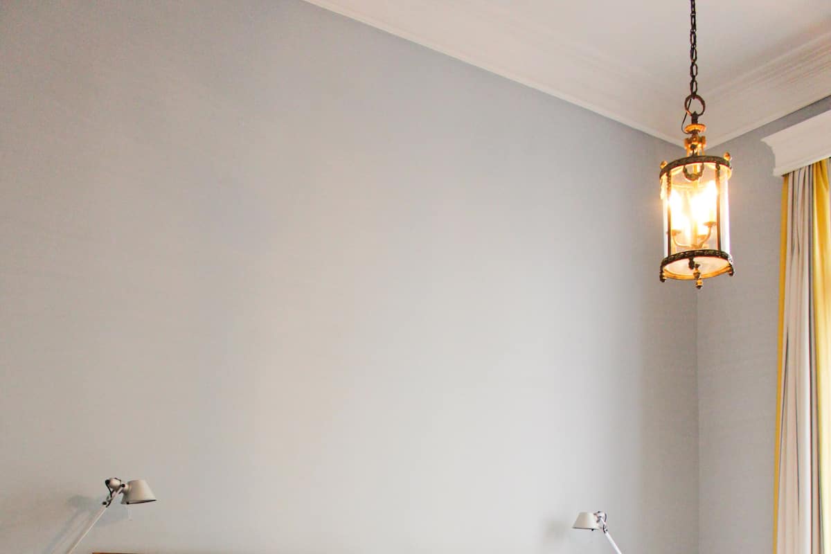 Quarto de hotel com duas camas, cabeceiras de madeira, luminárias de mesa e uma cadeira de madeira, além de um pendente.