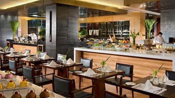 Um restaurante moderno com várias mesas, um balcão central com diversos tipos de comida e um cozinheiro a preparar refeições.