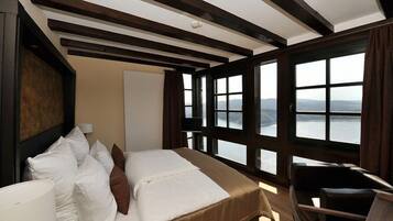Quarto com cama, escrivaninha e grandes janelas com vista para o exterior.