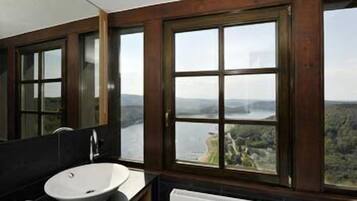 Casa de banho com uma grande janela que oferece uma vista panorâmica de um vale e um lago.
