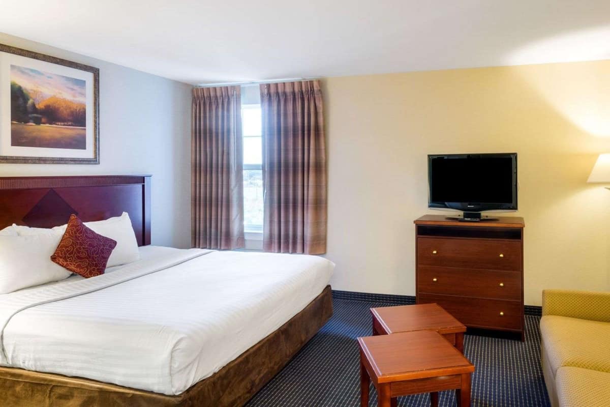 Quarto de hotel com cama, televisão, penteadeira, cadeira e uma pequena mesa.