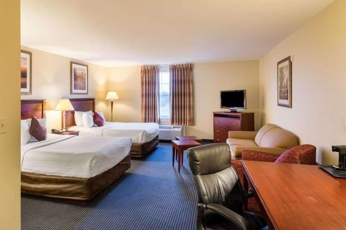 Quarto de hotel com duas camas, uma escrivaninha, uma cadeira, uma televisão e uma janela com cortinas.