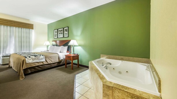 Quarto de hotel com cama, duas mesas de cabeceira com luminárias, uma banheira grande e paredes verdes.