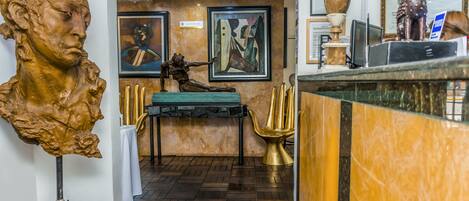 Uma área de recepção com balcão de mármore, busto de bronze e obras de arte emolduradas nas paredes.
