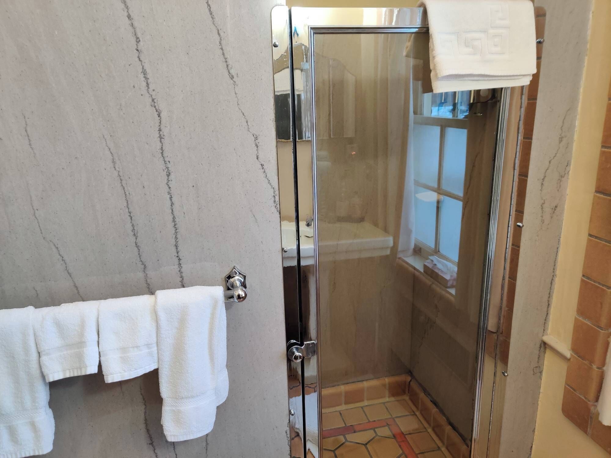 Um banheiro com box de vidro, parede de mármore e piso revestido com azulejos.
