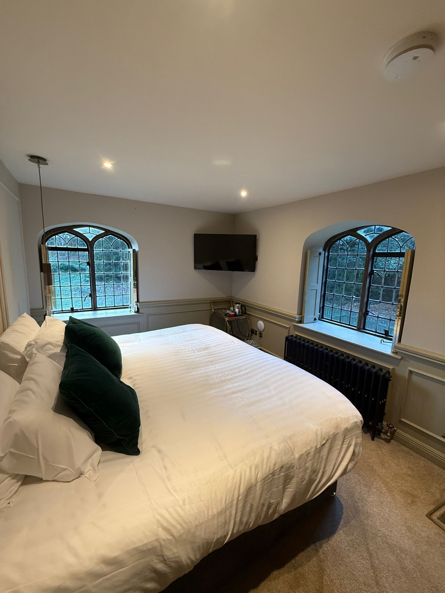 Quarto com cama grande, duas janelas, radiador e televisão de tela plana na parede.
