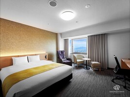 Quarto de hotel com cama grande, cadeira de massagem, escrivaninha e vista para a cidade pela janela.
