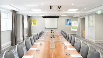 Uma sala de conferência com uma mesa comprida, cadeiras e uma tela de projeção.