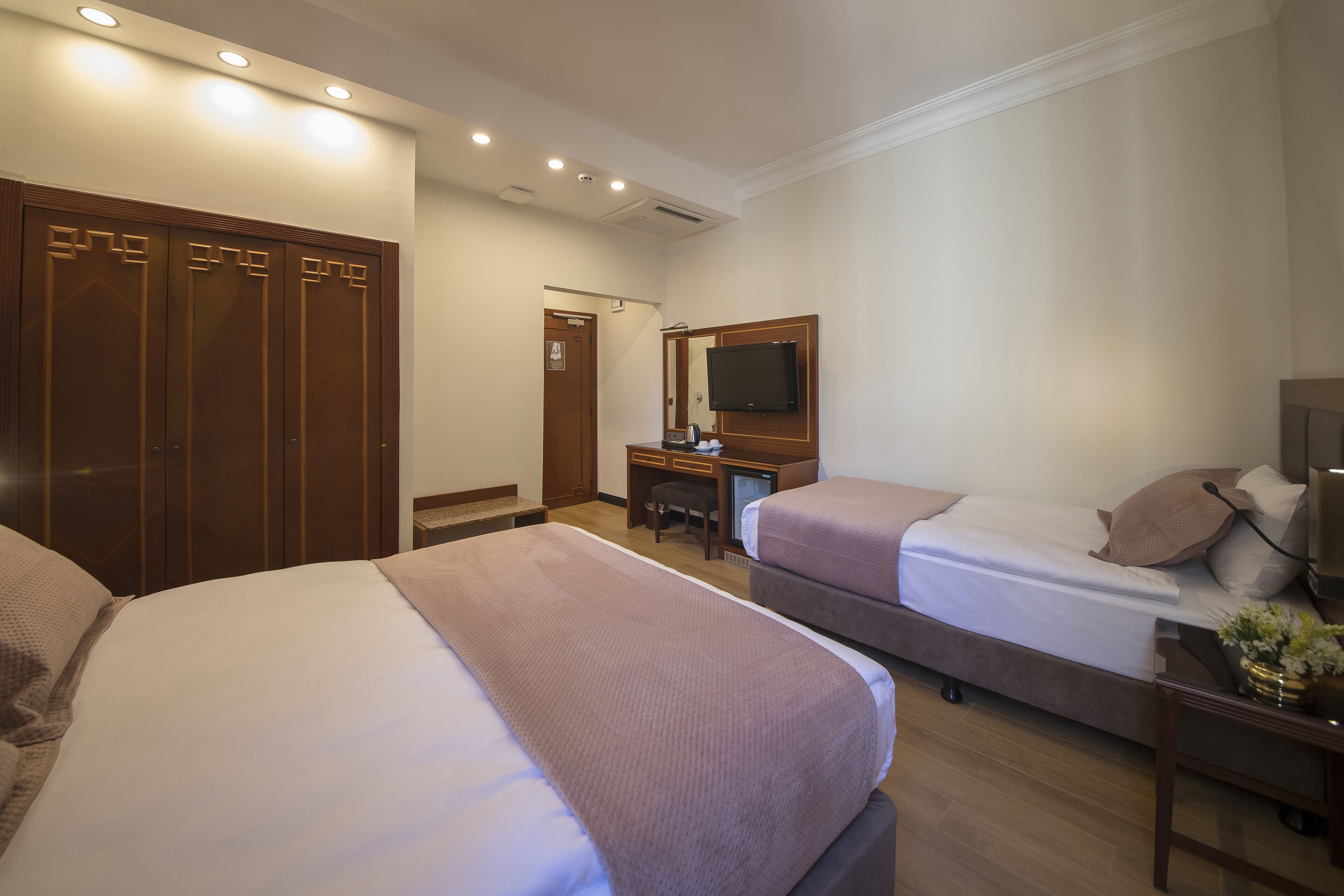 Quarto de hotel com duas camas, uma escrivaninha com cadeira, televisão e um guarda-roupa.