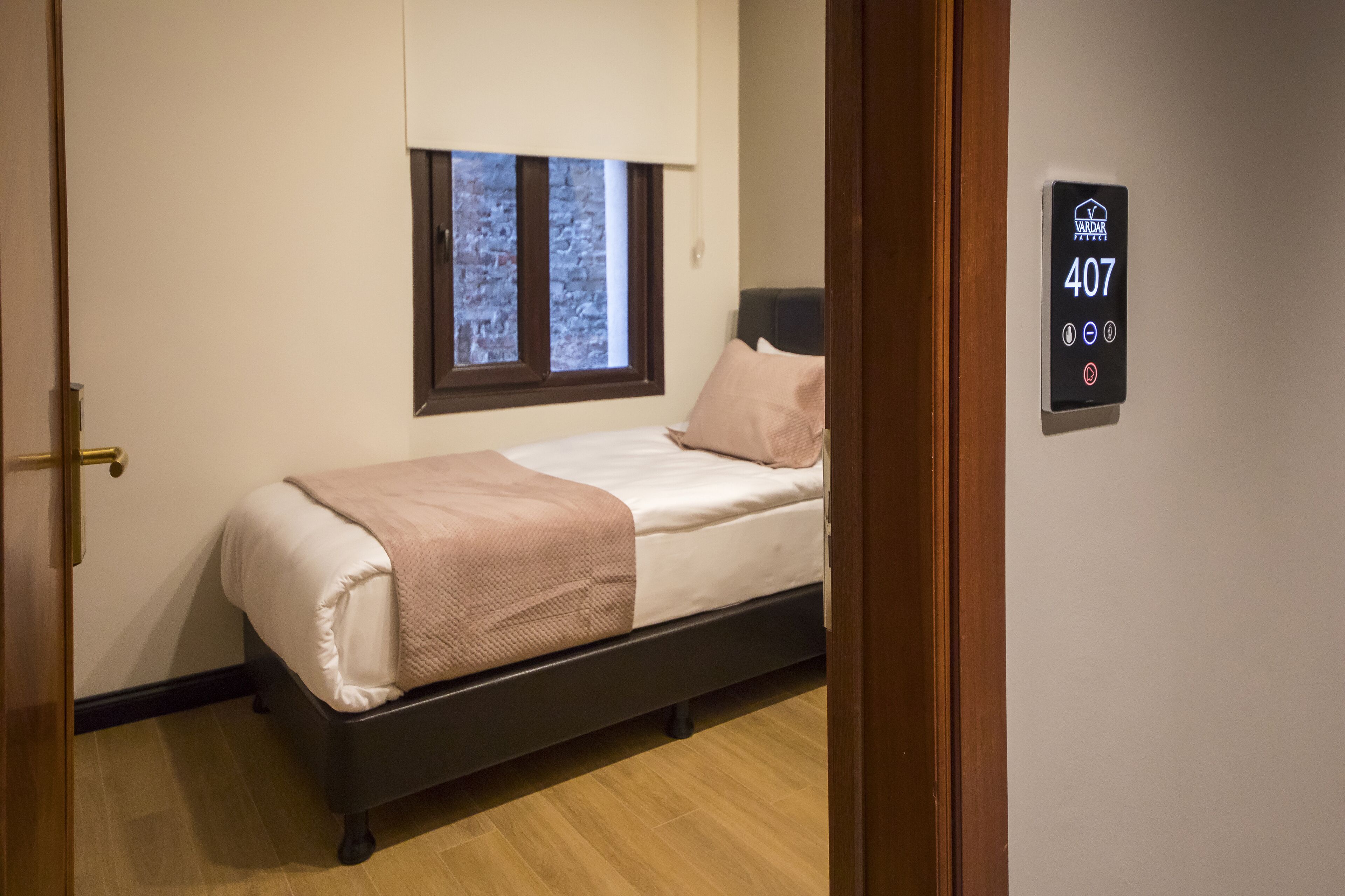 Quarto de hotel com uma cama, uma janela e uma fechadura digital mostrando o número 407.