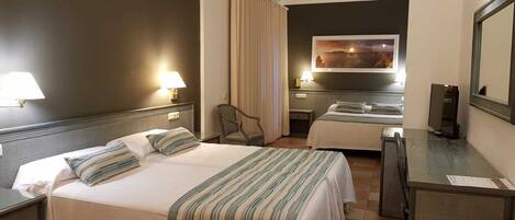Quarto de hotel com duas camas, uma escrivaninha, uma cadeira, um espelho e um quadro na parede.