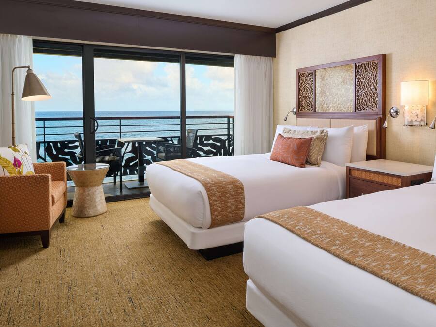 Quarto de hotel com duas camas, um sofá, uma mesa pequena e varanda com vista para o mar.