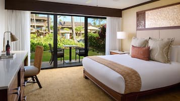 Quarto de hotel com uma cama grande, uma escrivaninha, uma cadeira e vista para um resort com palmeiras e piscina.