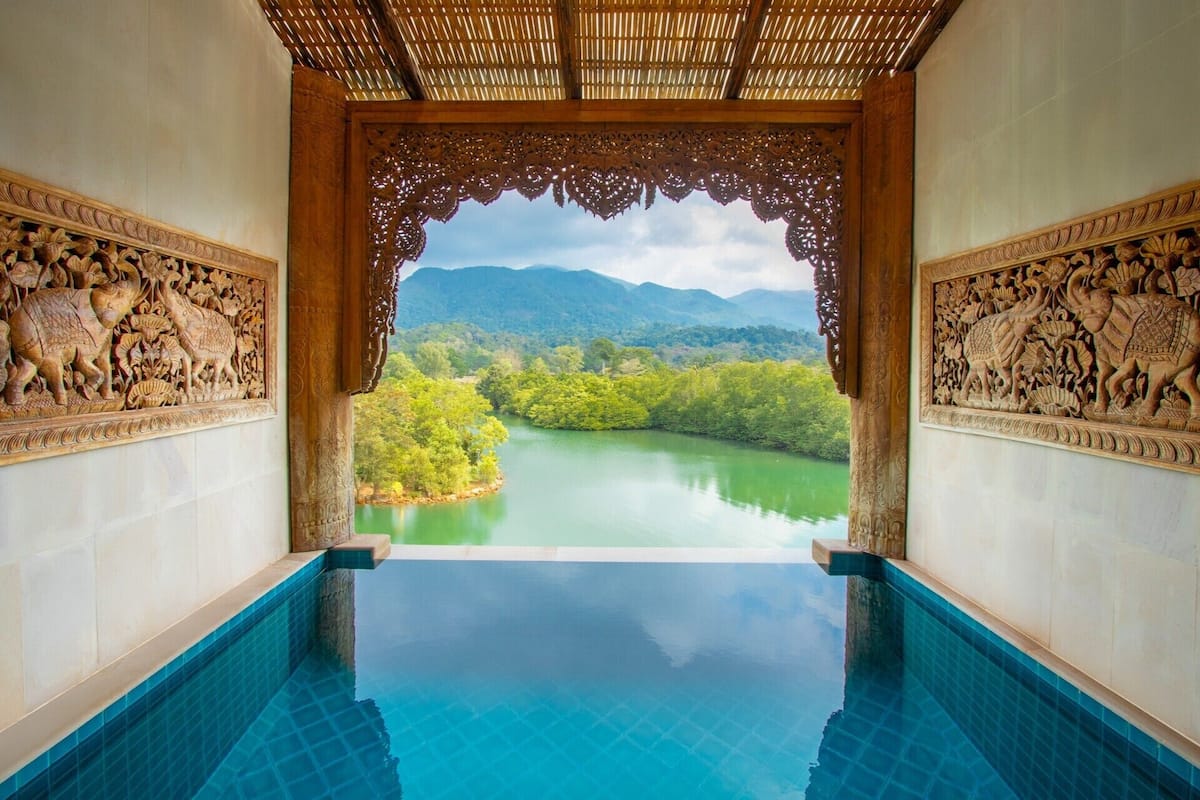 Piscina infinita com vista para um rio verde e montanhas.