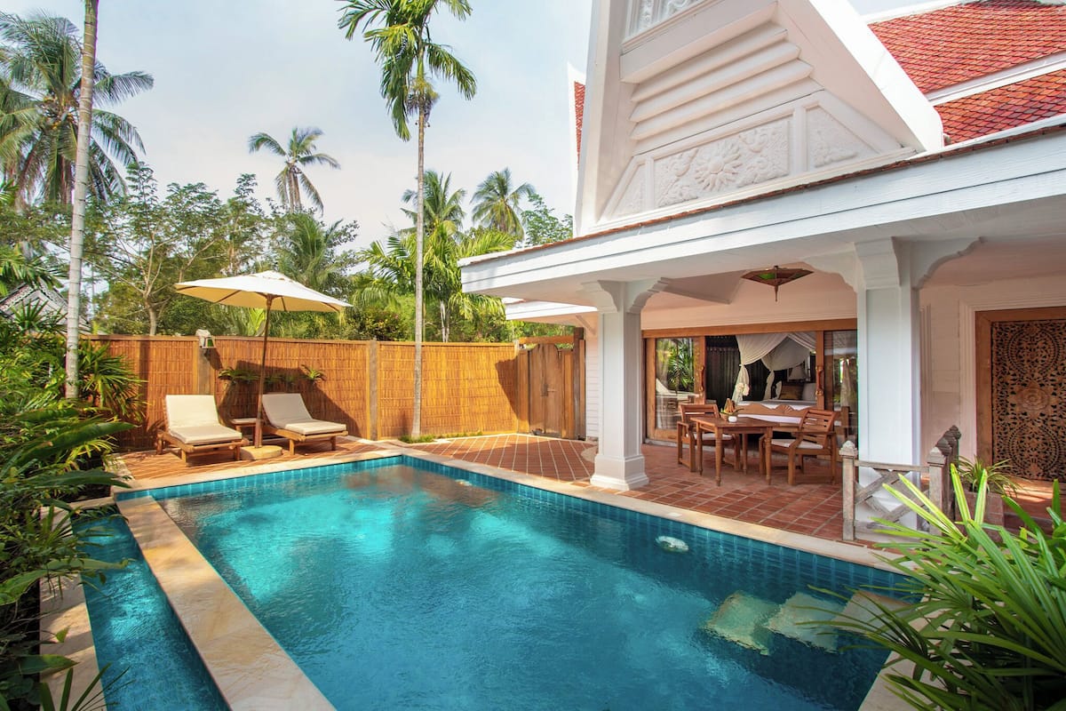 Piscina com espreguiçadeiras e guarda-sóis, cercada por vegetação tropical e um cercado de madeira.