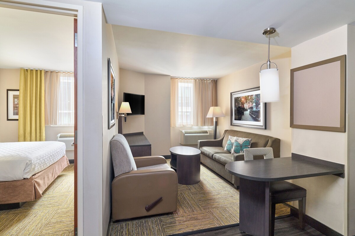 Quarto de hotel com cama, sofá, escrivaninha e televisão.