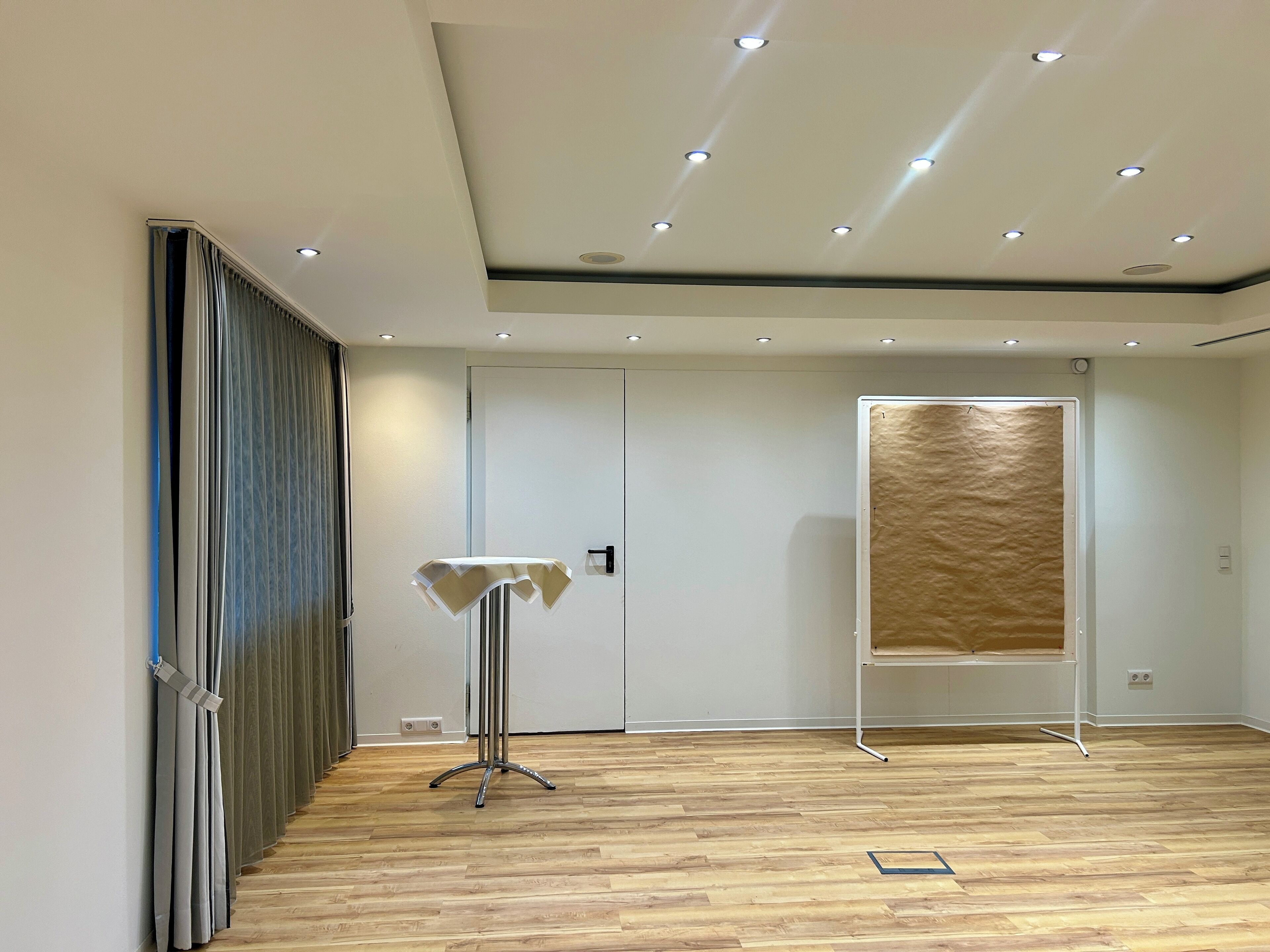 Quarto de hotel moderno com piso de madeira, um quadro de apresentações, uma luminária de mesa e uma porta com painel texturizado.