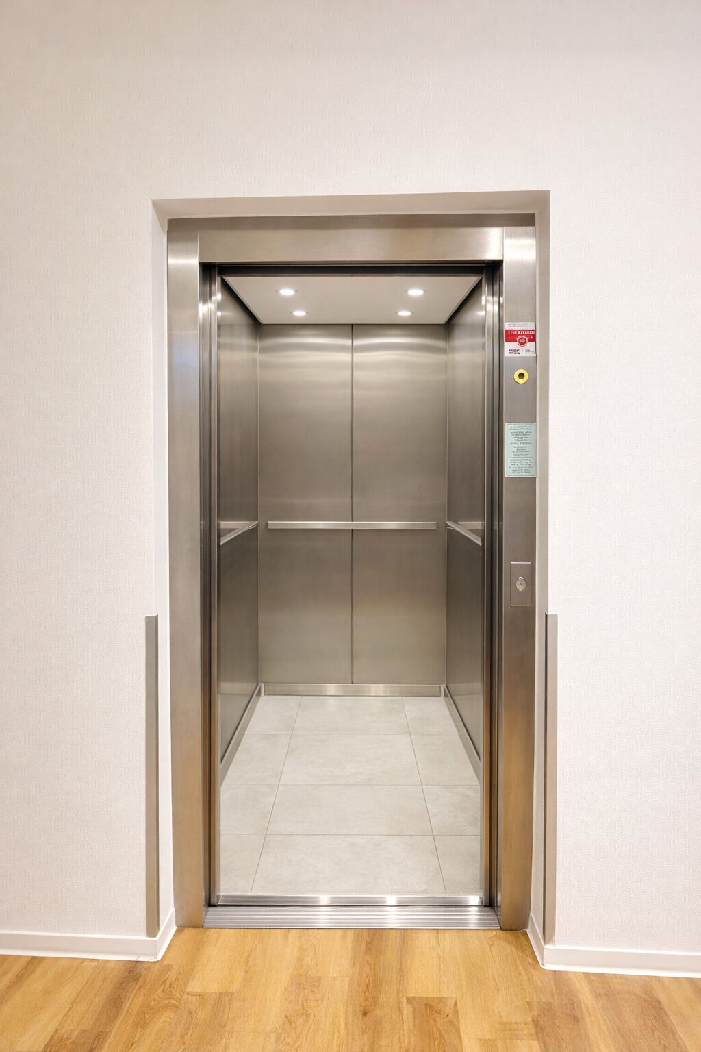 Um elevador com interior metálico, painel de comando e placa de saída de emergência.