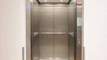 Um elevador com interior metálico, painel de comando e placa de saída de emergência.