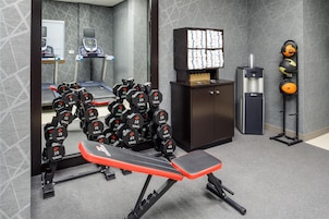 Uma academia com equipamentos de musculação, esteiras e um bebedouro.