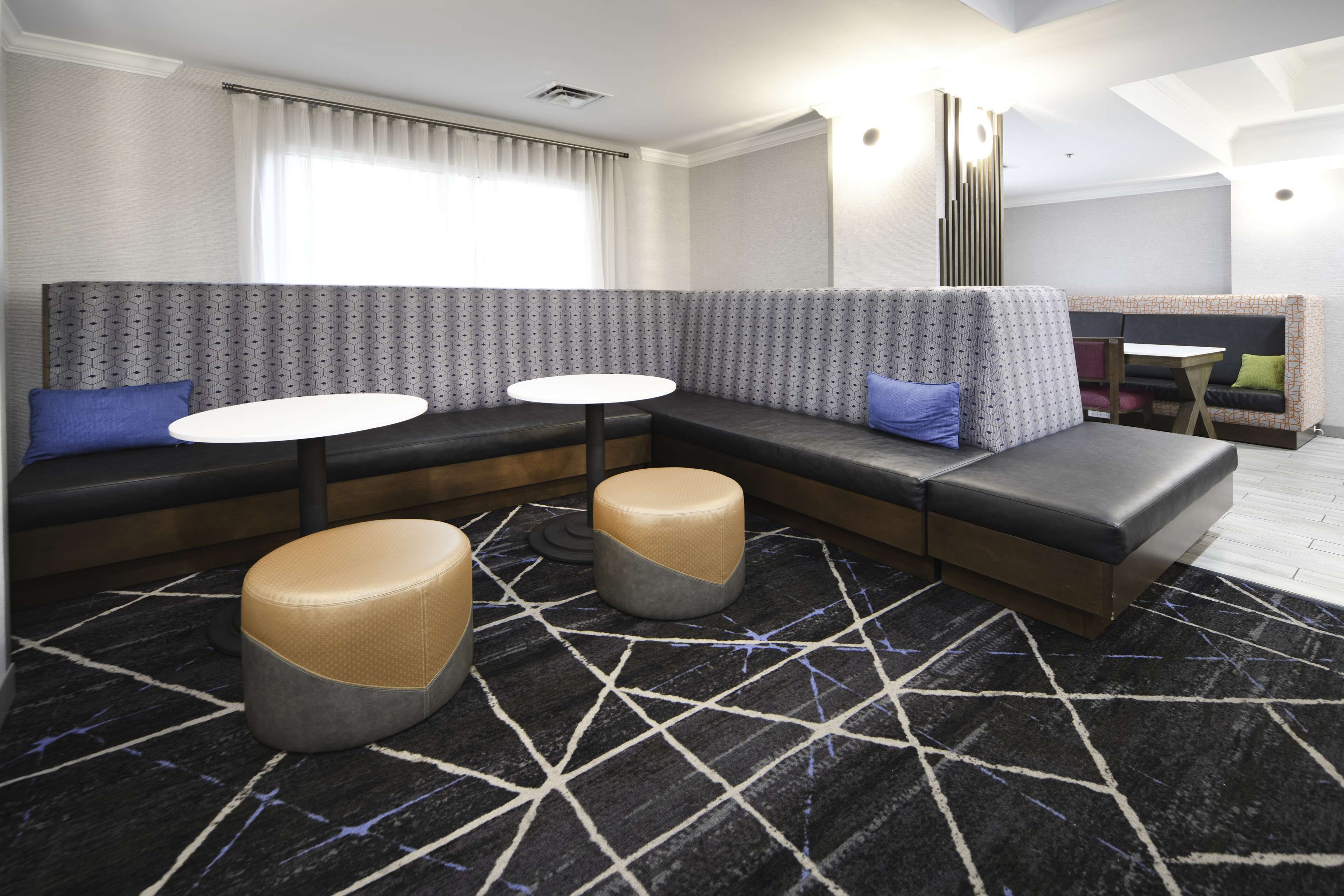 Quarto de hotel moderno com sofá modular, duas mesas redondas e pufes.