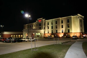 Hotel com vários andares, placa visível, estacionamento e fachada bem iluminada.