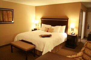 Quarto de hotel com uma cama grande, duas mesas de cabeceira, um banco e uma cadeira.