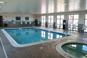 Piscina interior com água cristalina, rodeada por espreguiçadeiras e chão revestido de azulejos.