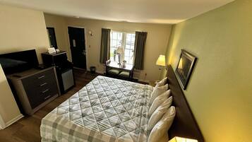 Quarto de hotel com cama, escrivaninha, televisão e janela com cortinas.