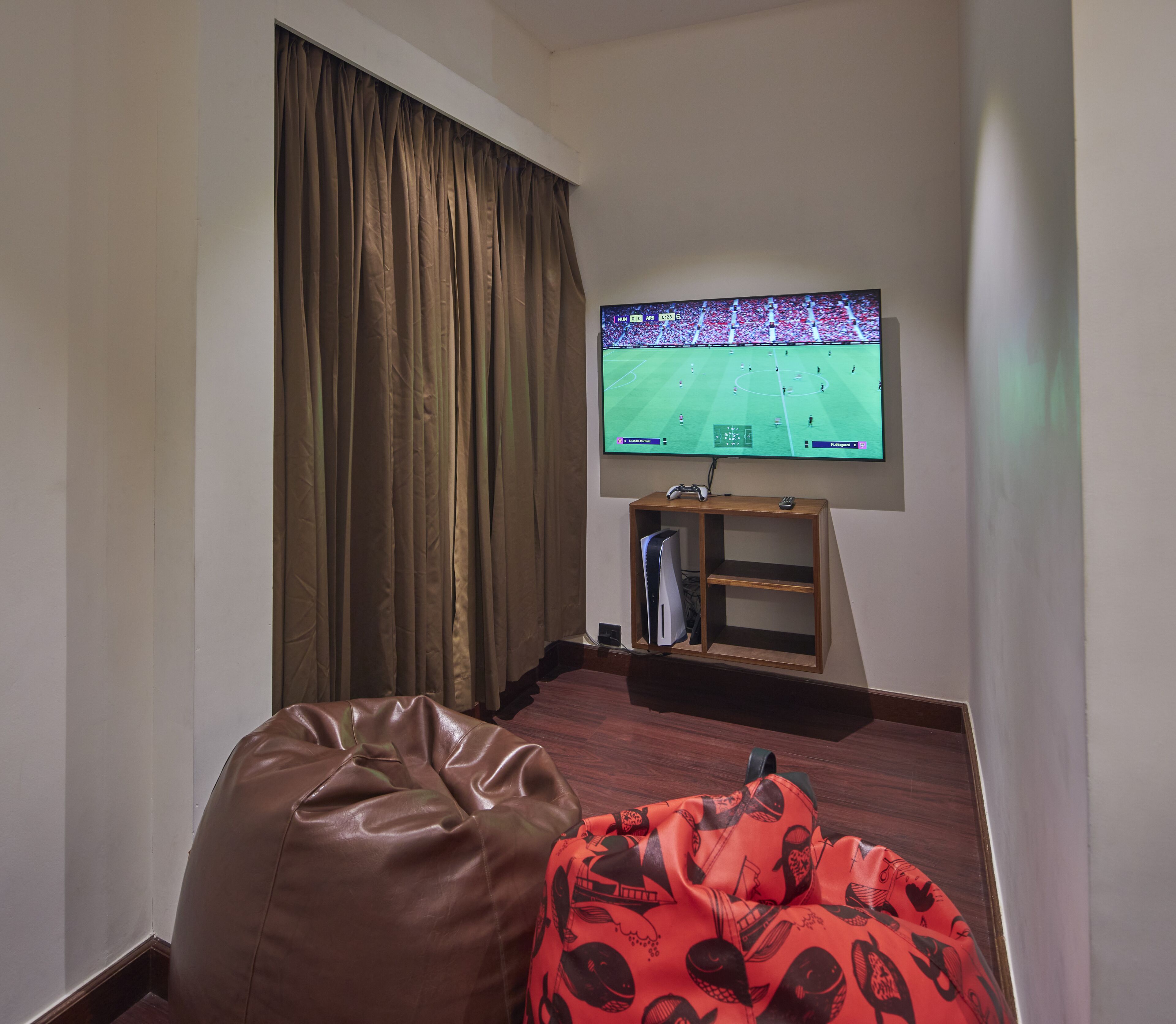 Quarto com televisão exibindo uma partida esportiva, uma poltrona de milho e uma prateleira de madeira com um console de jogos.
