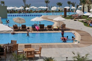 Área de piscina com espreguiçadeiras, guarda-sóis e deck de madeira.