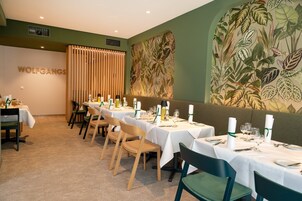 Restaurante com mesas preparadas para refeições, parede com mural botânico e um letreiro com a inscrição "WOLFGANGS".