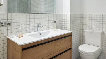 Casa de banho moderna com toucador de madeira, lavatório branco e sanita.