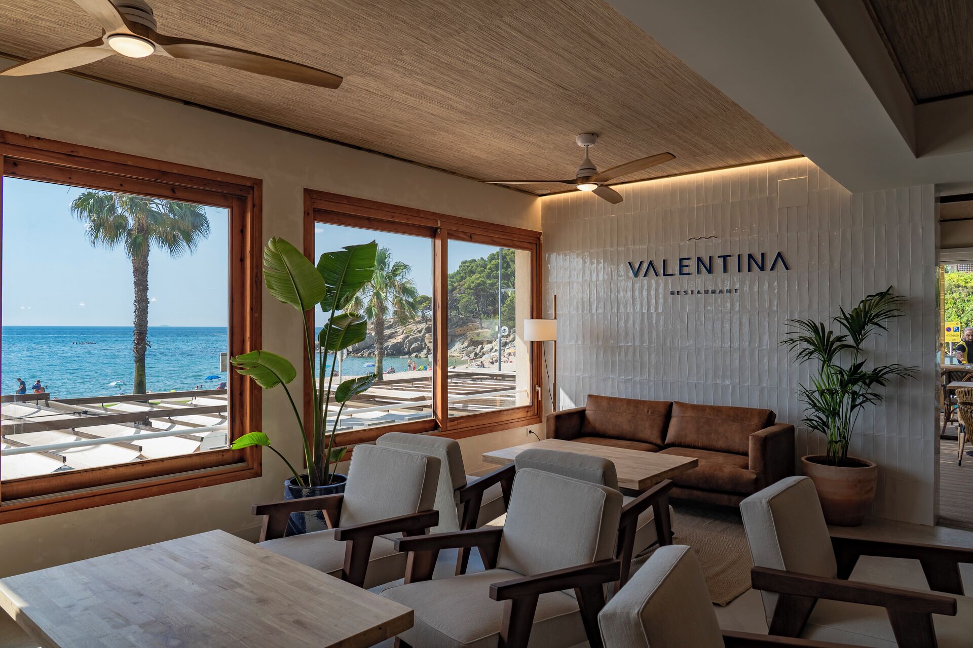 Interior de restaurante com vista para a praia, um ventilador de teto e uma placa com o nome "Valentina Restaurant".