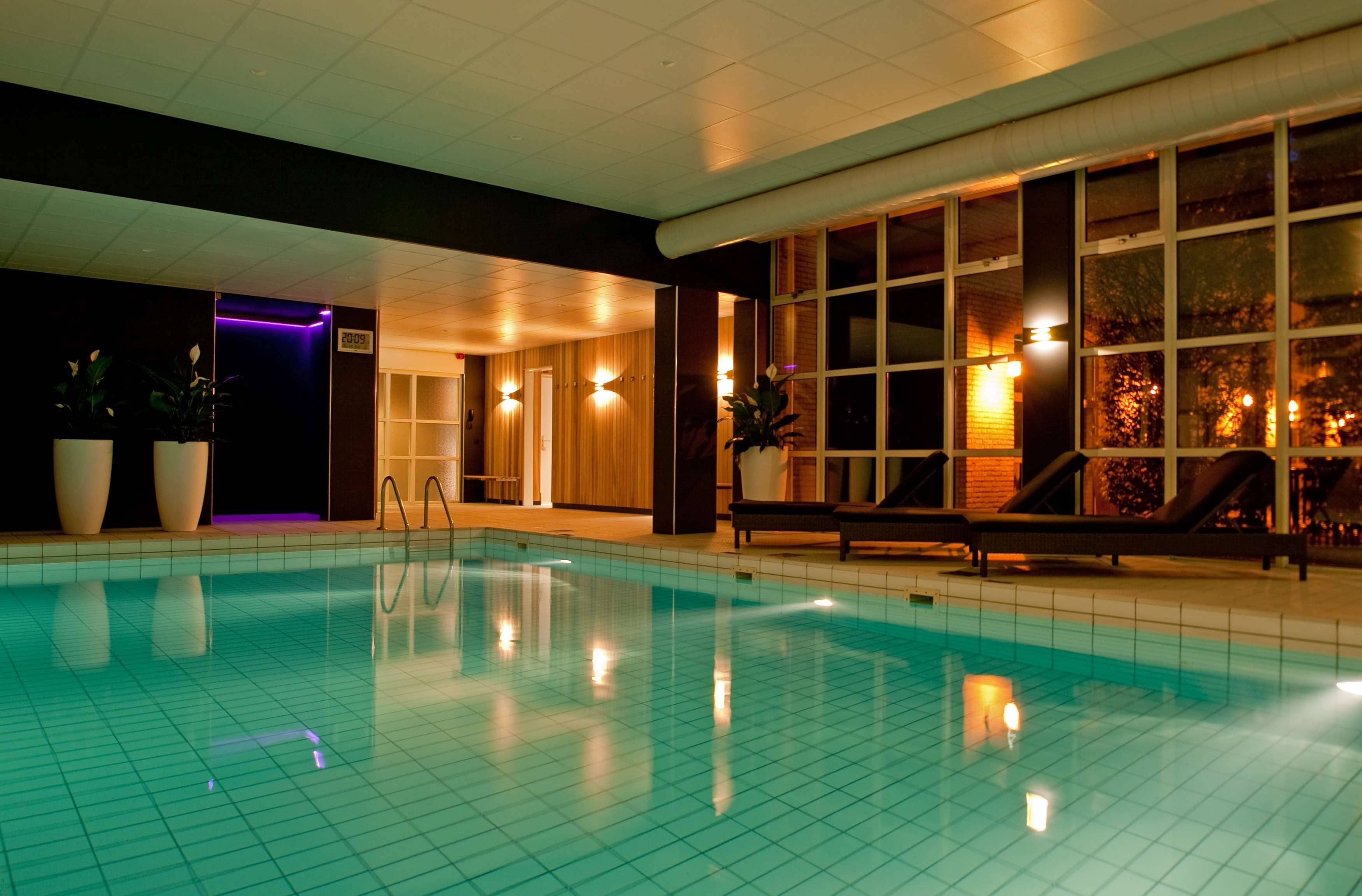 Piscina interna com piso ladrilhado, um banco e uma janela com vista para árvores.