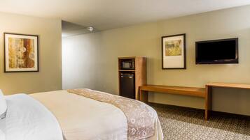Quarto de hotel com cama, escrivaninha, micro-ondas e televisão.
