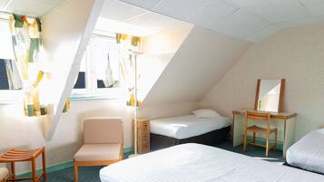 Um quarto pequeno e triangular com uma cama, uma cadeira, uma escrivaninha e um espelho.