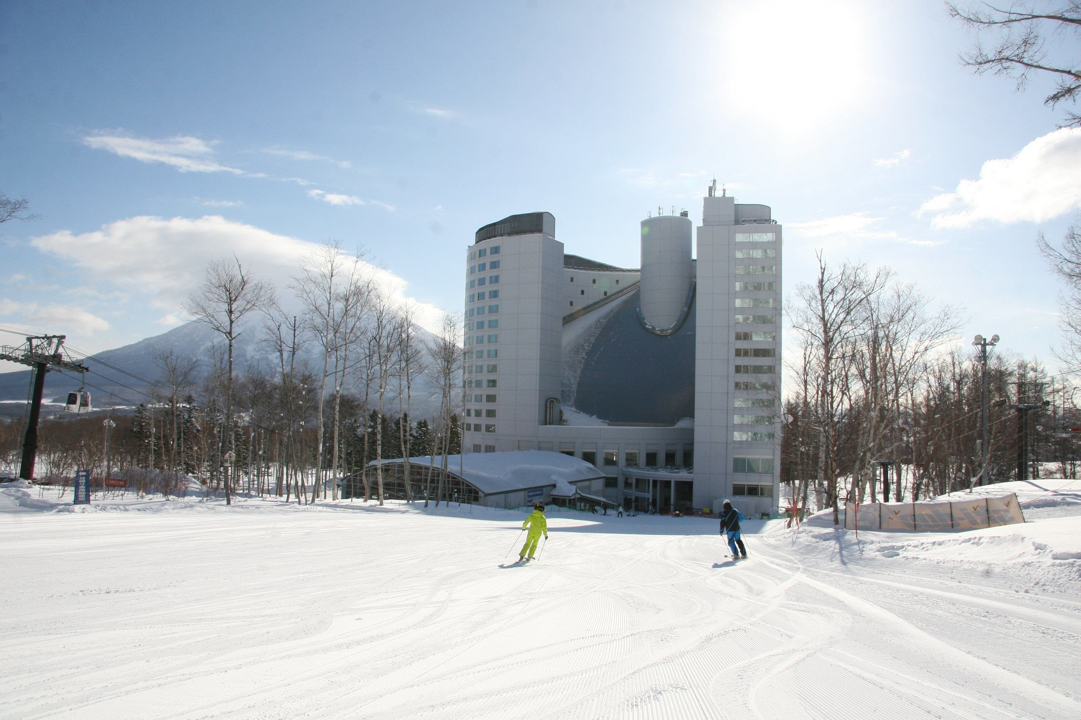 Estância de esqui com um edifício grande, terreno coberto de neve e uma montanha ao fundo.