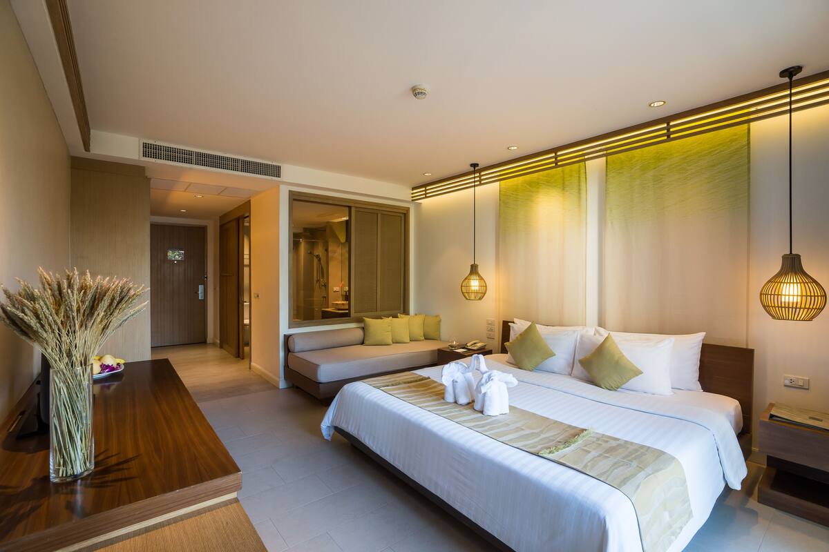 Quarto de hotel moderno com uma cama grande, um sofá, uma escrivaninha e um espelho.