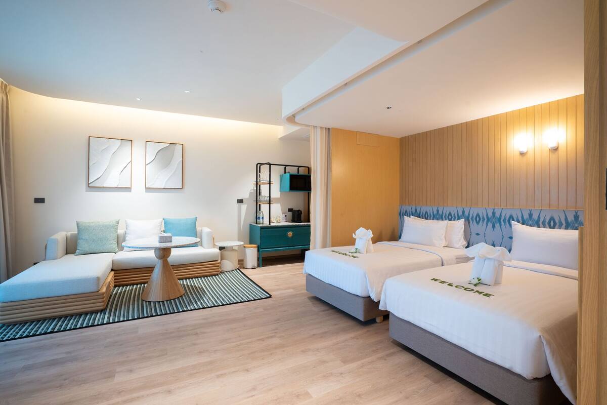 Quarto de hotel moderno com duas camas, um sofá, uma mesa de centro e uma pequena escrivaninha.