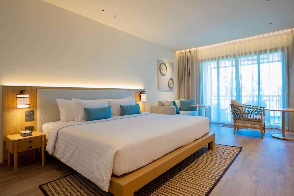 Quarto de hotel moderno com uma cama grande, mesas de cabeceira, um sofá, uma poltrona e uma pequena mesa.