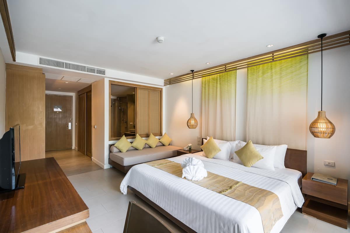 Quarto de hotel moderno com uma cama grande, um sofá-cama, uma escrivaninha de madeira e uma televisão.