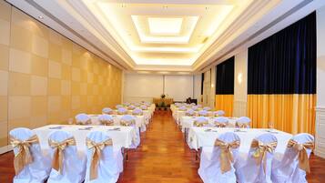 Uma sala de banquetes com mesas dispostas em fileiras, toalhas brancas e cadeiras com fitas douradas.