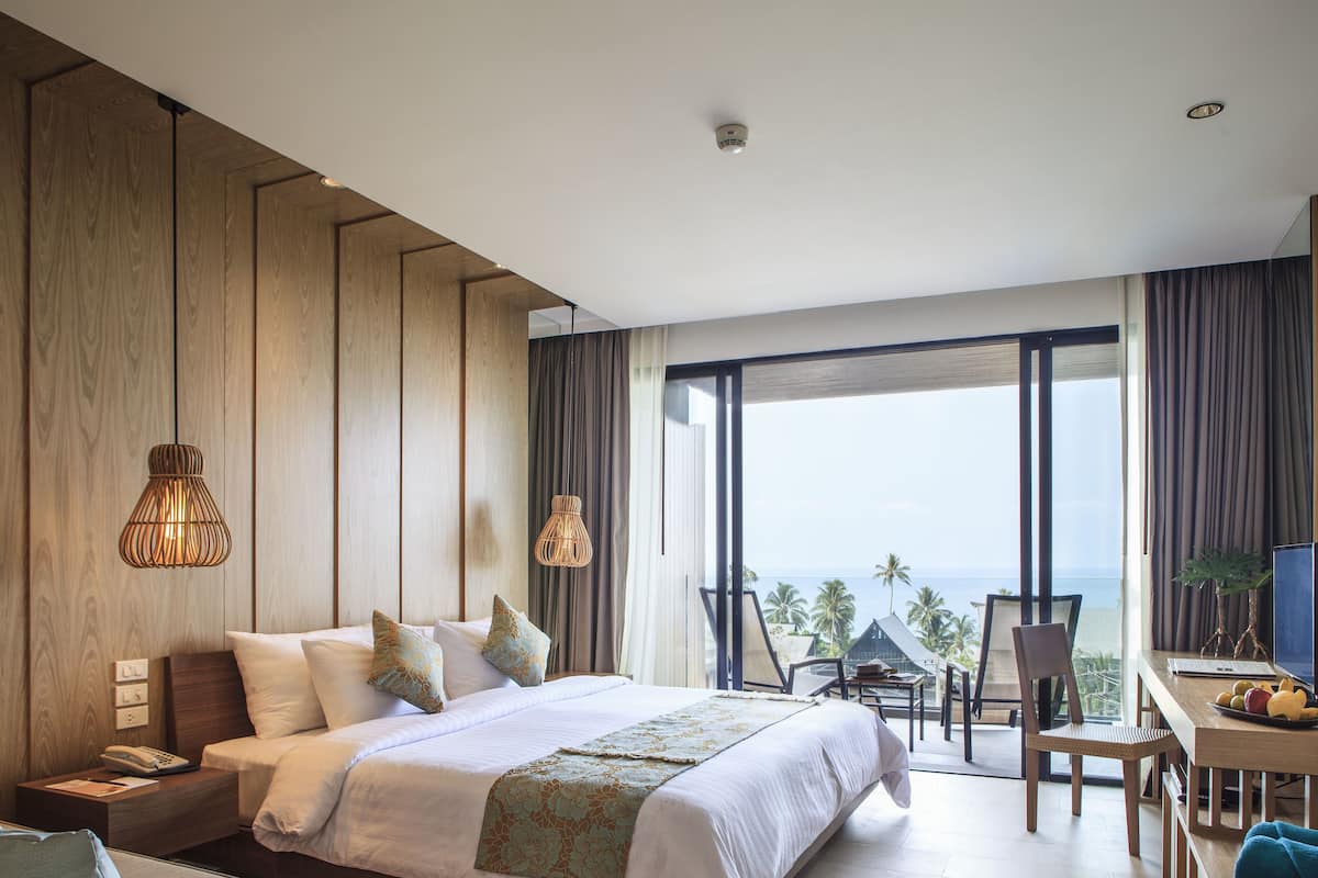 Quarto de hotel moderno com uma cama grande, uma escrivaninha e varanda com vista.